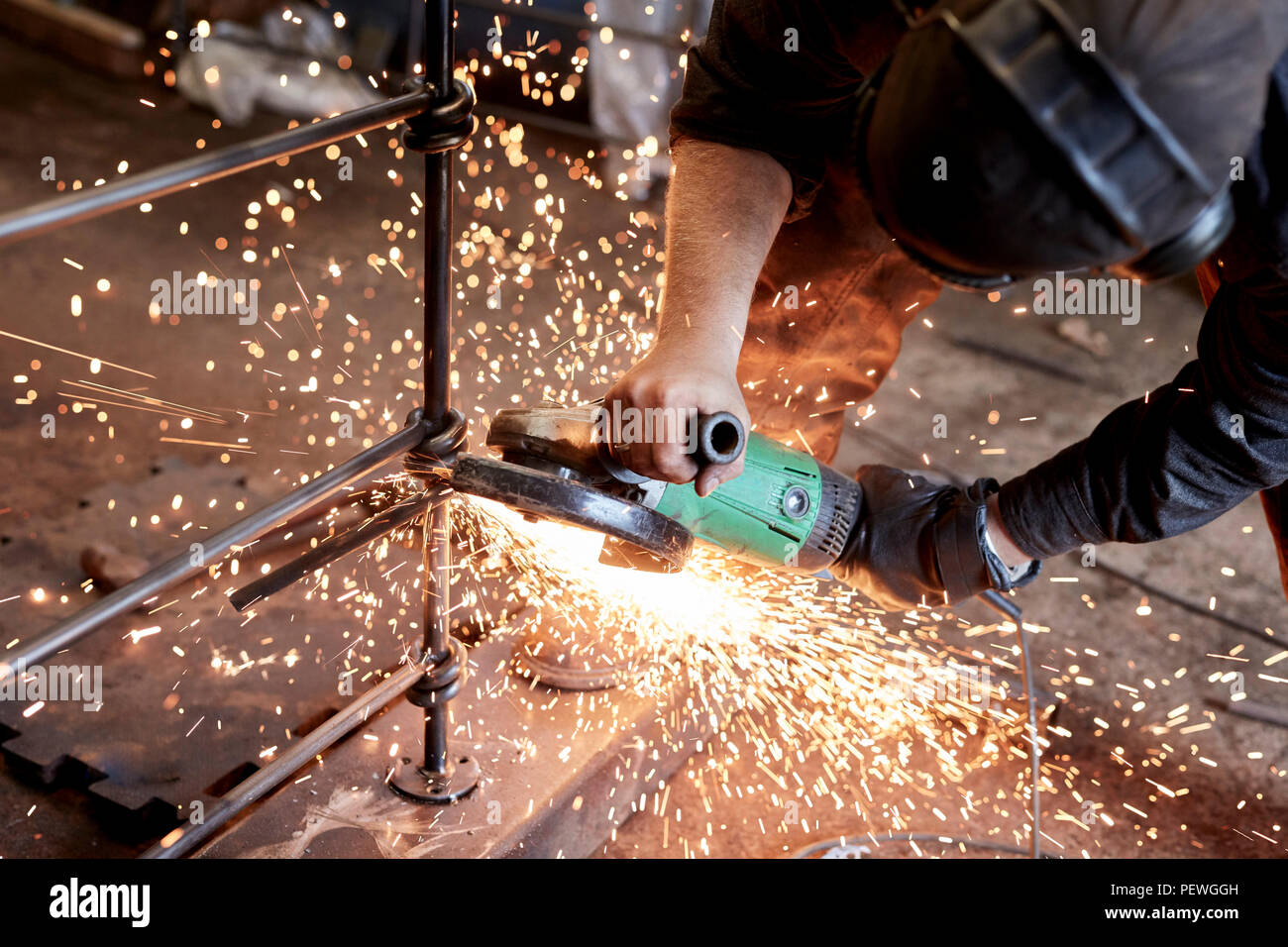 An artisan metalworker at work holding an angle grinder, workng on a ...
