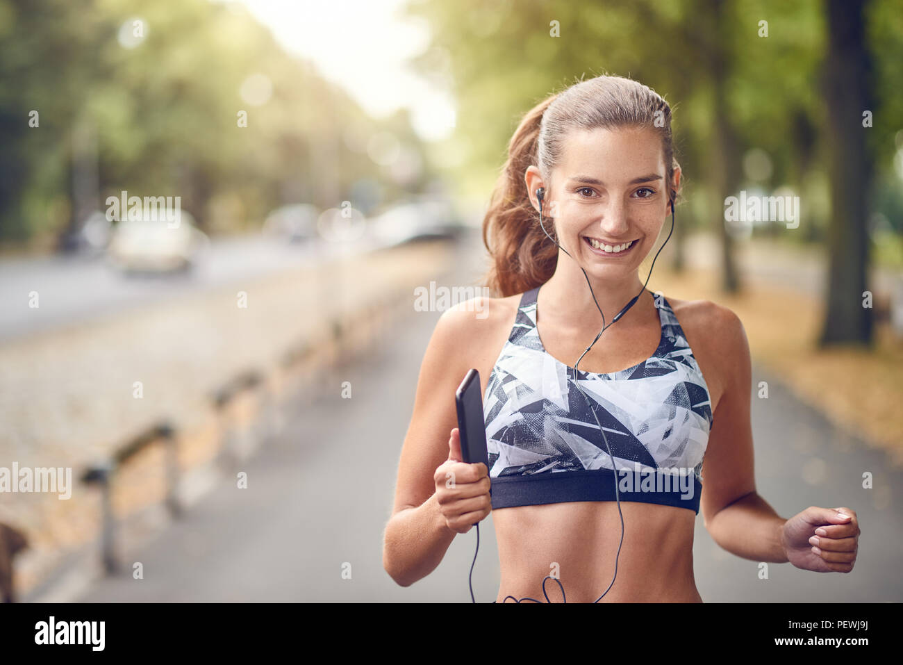 Fit healthy athletic woman jogging on a river bank smiling happily with ...