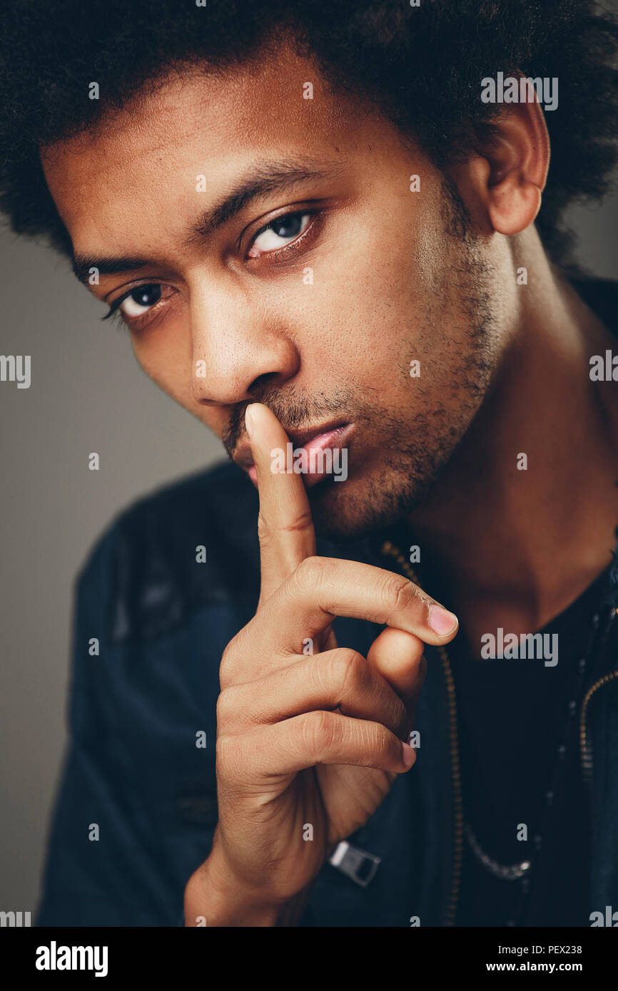 Top secret. Young African man holding a finger on his lips, asking to ...