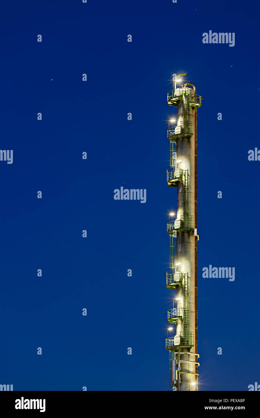 A tall distillation tower isolated on blue night sky with a lot of ...