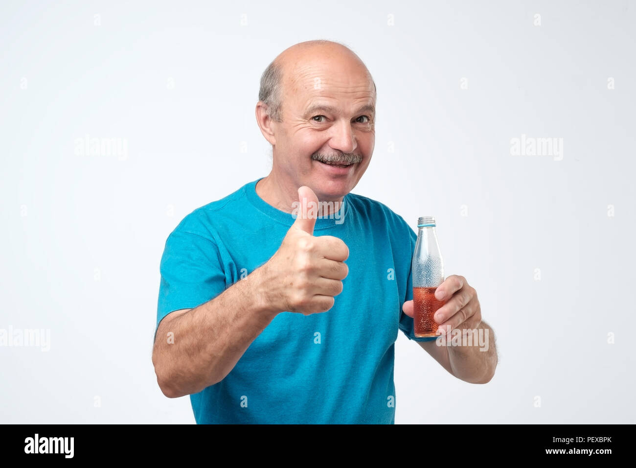 portrait of a healthy mature man drinking water from glass bottle after ...