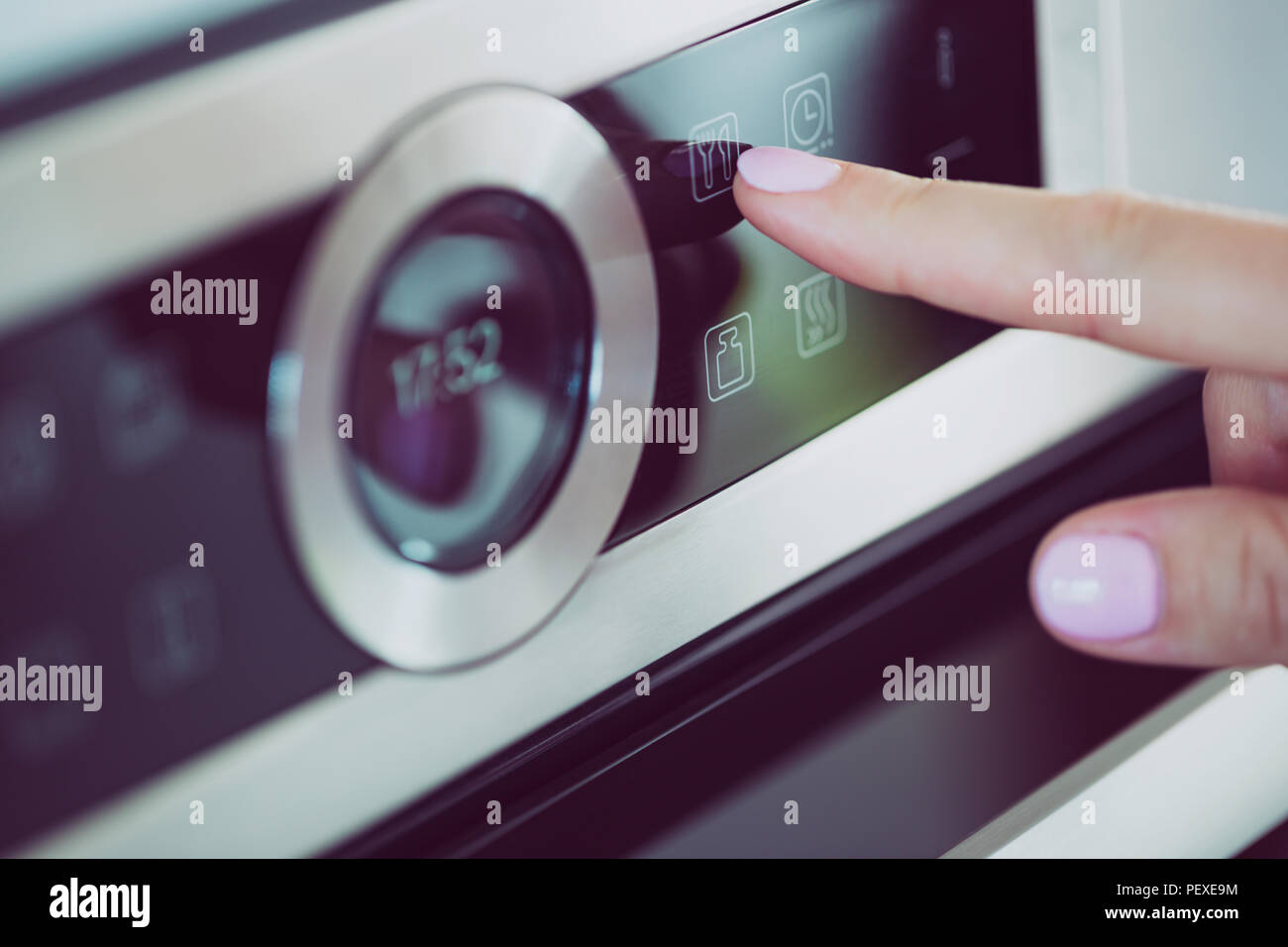 Female finger is touching the button of modern panel of electric oven ...