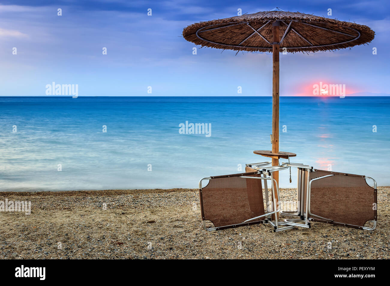 Straw beach parasol, two beach beds, sunset sky and silky, turquoise ...