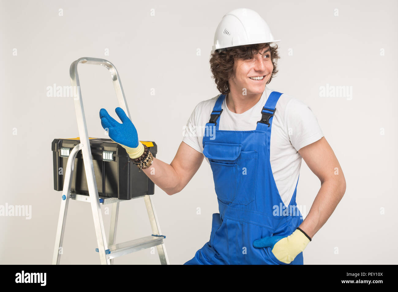 Studio portrait of handsome builder in white helmet and blue overall ...