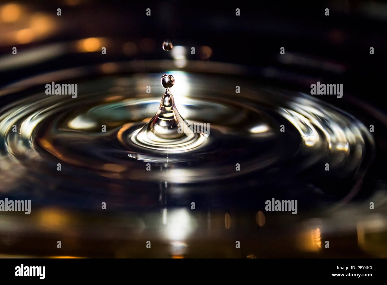 Silver drop jumping out of golden and blue illuminated water Stock ...