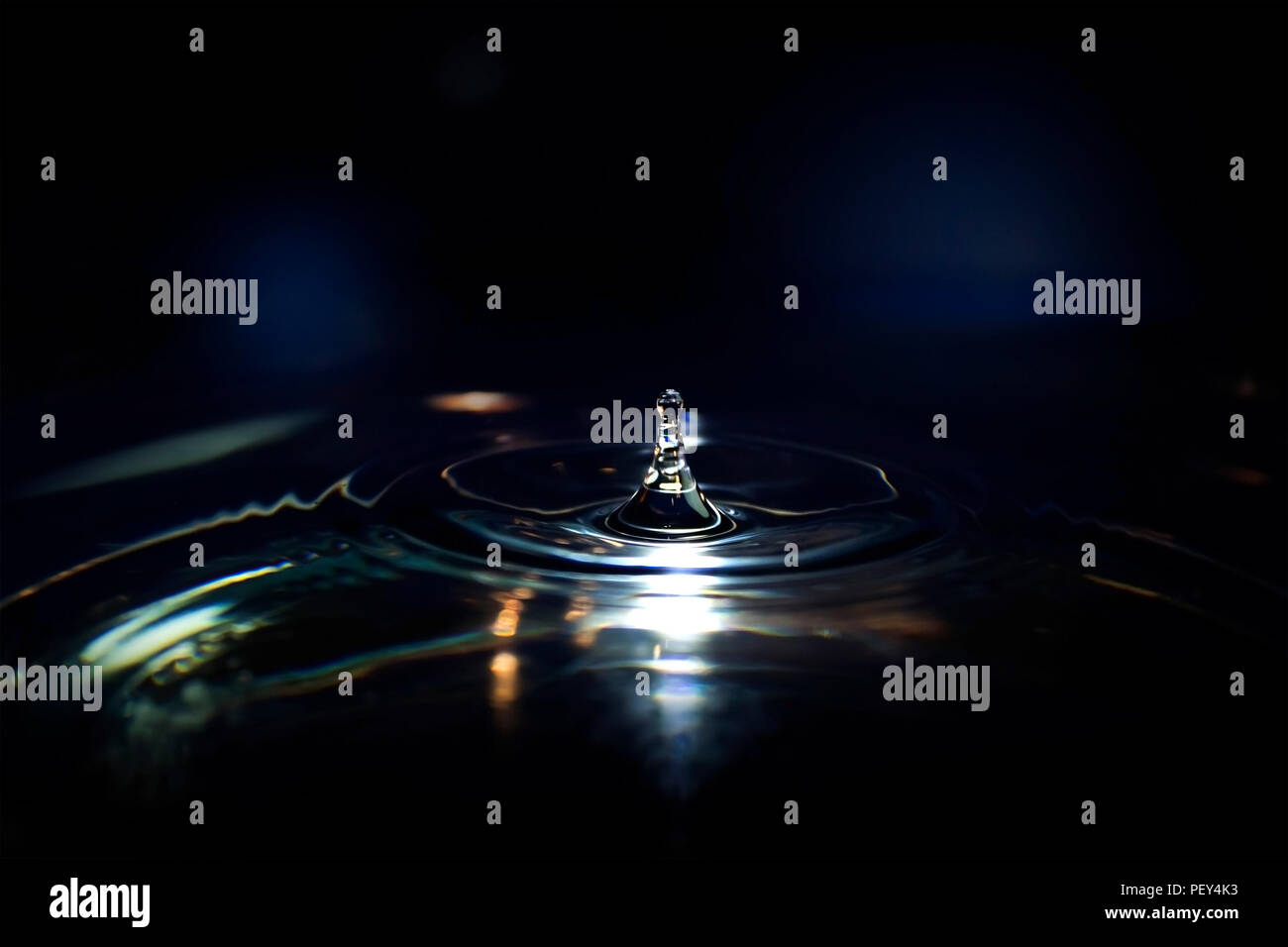 Symmetric drop jumping out of dark blue illuminated water at night ...
