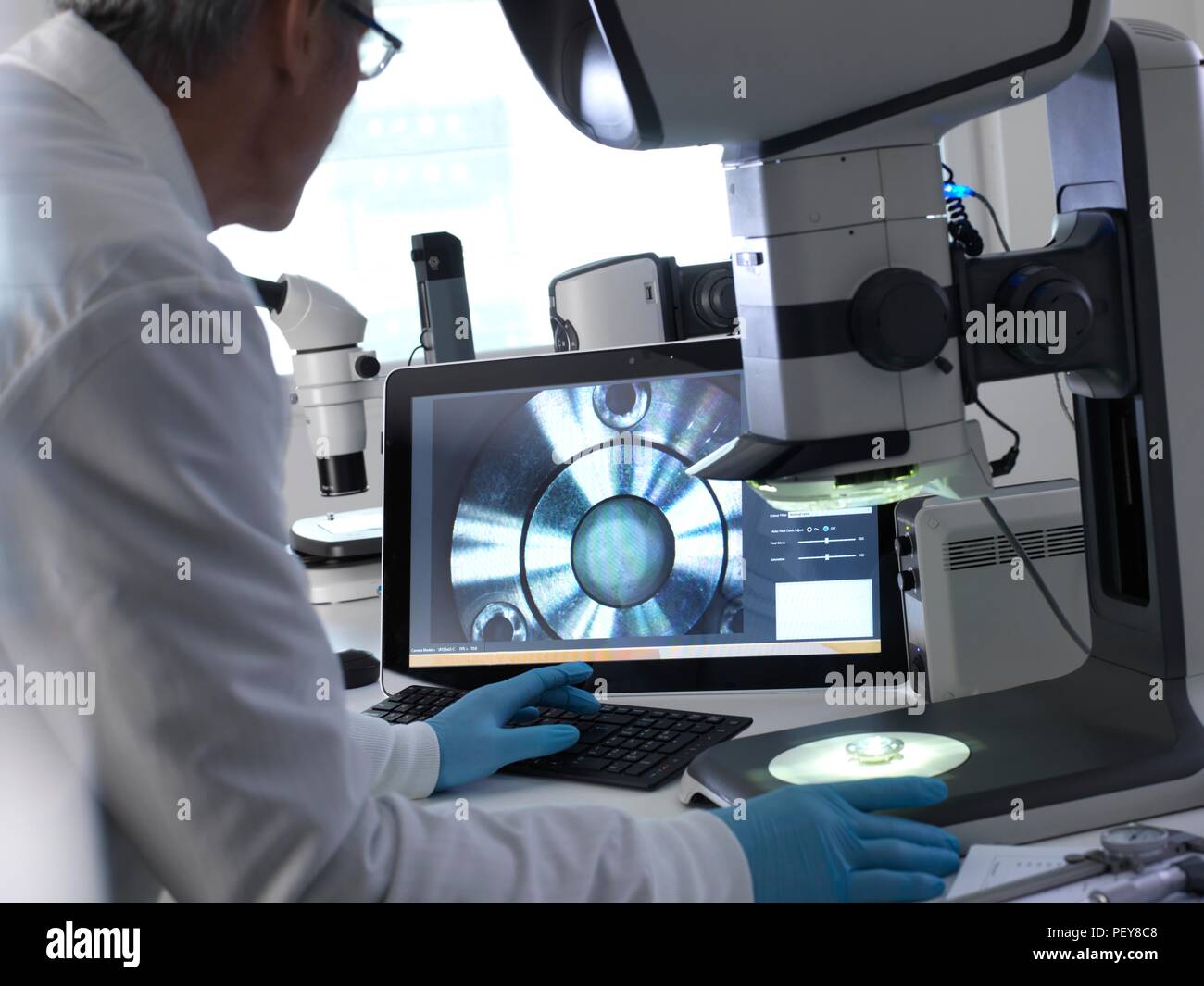 Engineer using a stereo microscope to inspect a manufactured component ...