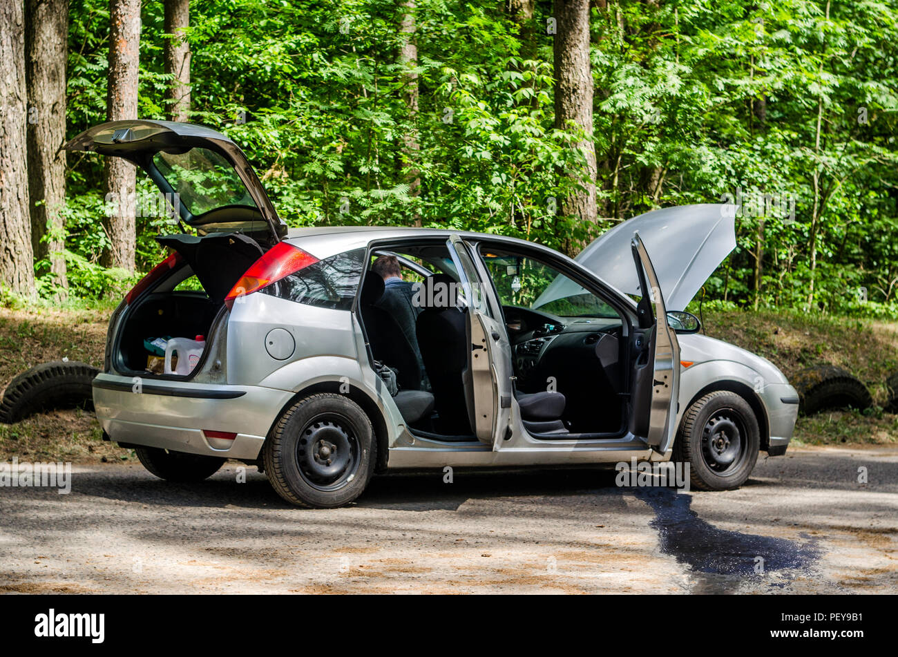 Broken car on the roadside with an open hood, trunk and doors. Oil leak ...