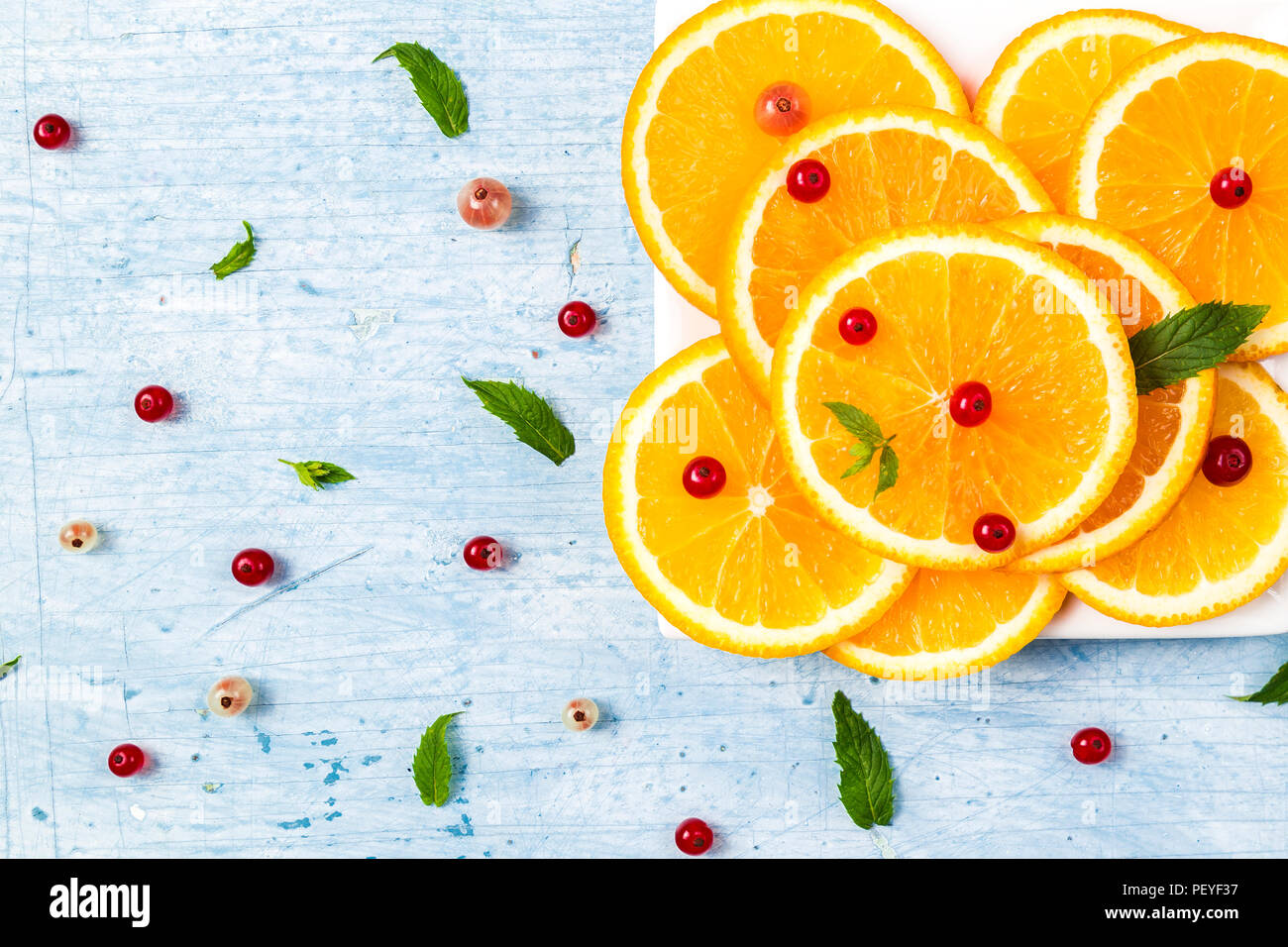 Slice orange with red currants and mint leaf on blue table background ...