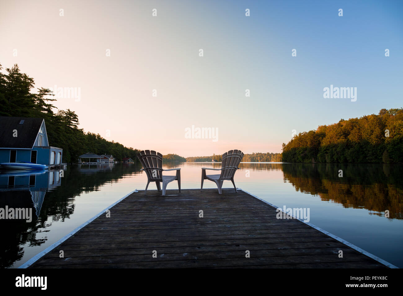 Muskoka chairs sitting at the end of a dock in front of Lake Joseph at ...