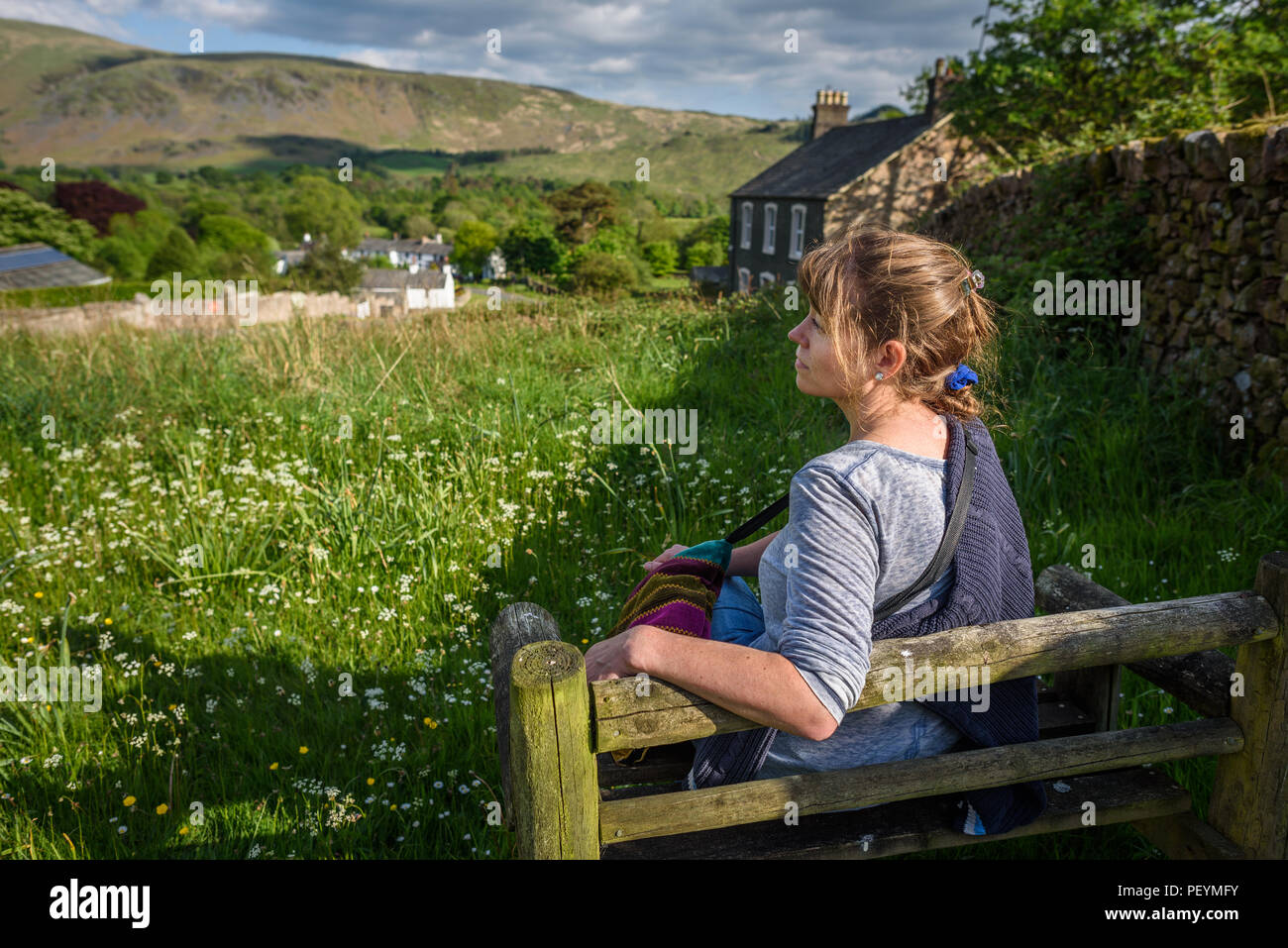 An attractive middle aged woman sat on a bench in sunlight enjoying ...