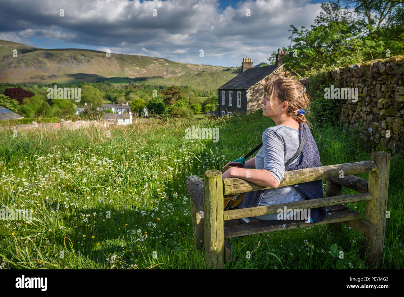 An attractive middle aged woman sat on a bench in sunlight enjoying ...