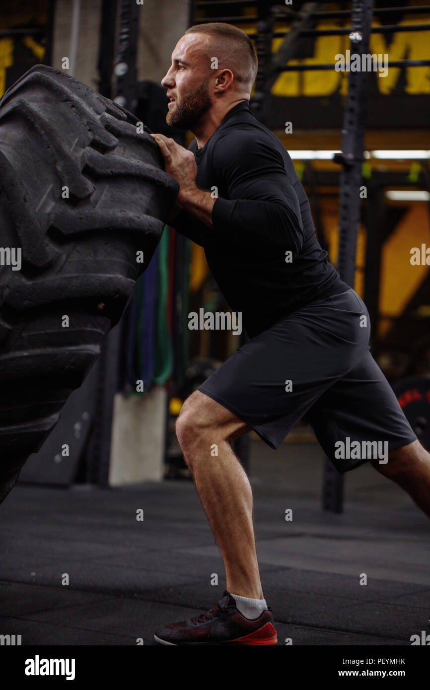 handsome bodybuilder with tensed muscles are raising the tire in the ...