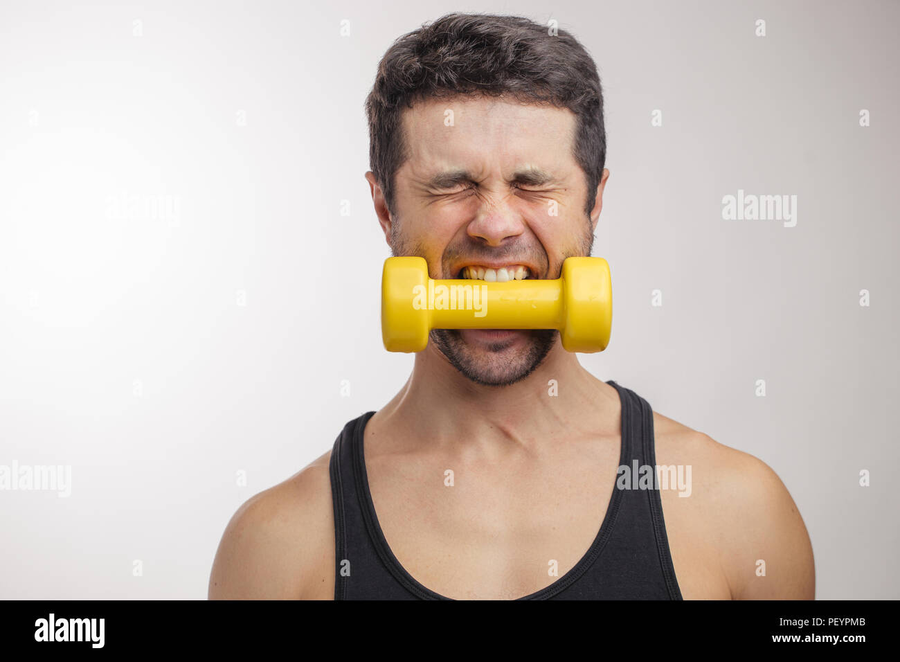 mad guy with a dumbbell clenched in his teeth. angry athlete. copy ...
