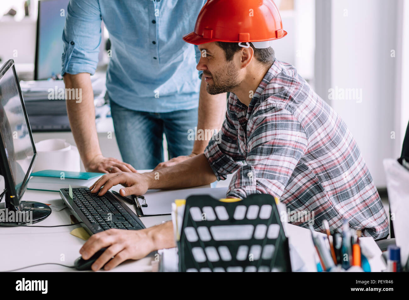 office worker wearing red hardhat is reviewing the plans on his ...