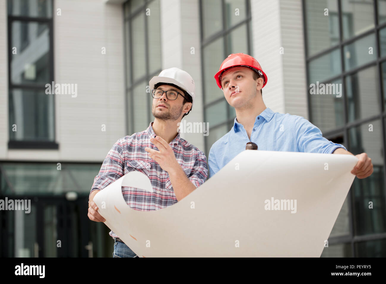 gorgeous engineers with blueprint are looking up. low angle view ...