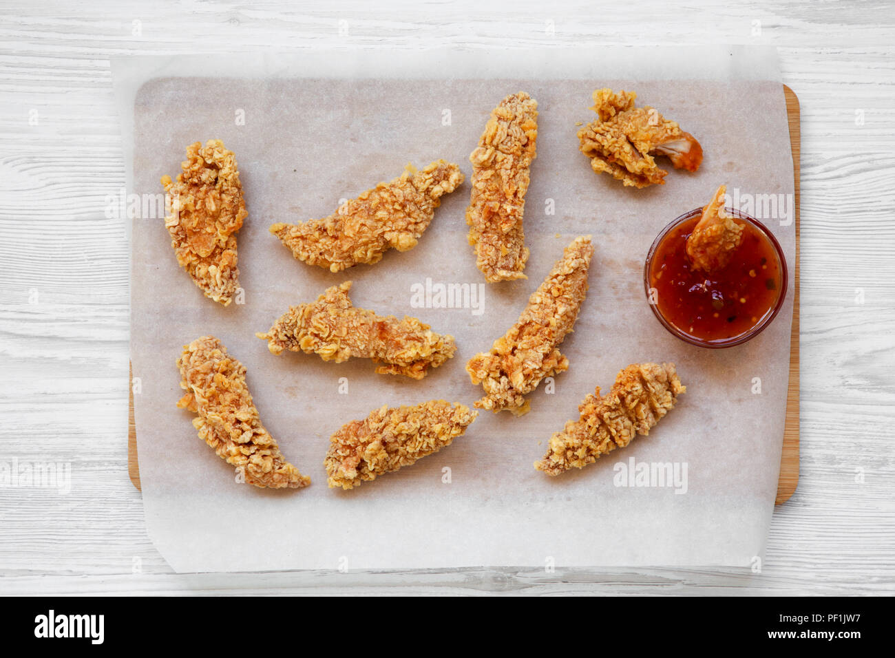 Overhead view chicken strips with sauce on bamboo board over white ...