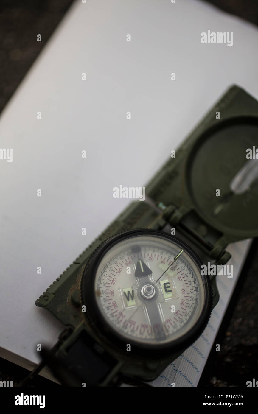 A lensatic compass and notepad are placed on the ground during ground ...