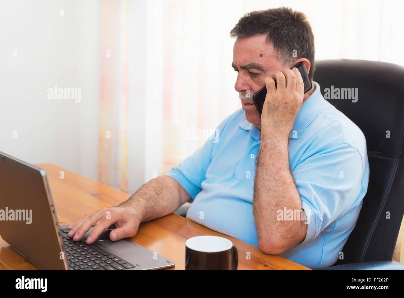 Angry senior man working on laptop while talking on the phone. Negative ...
