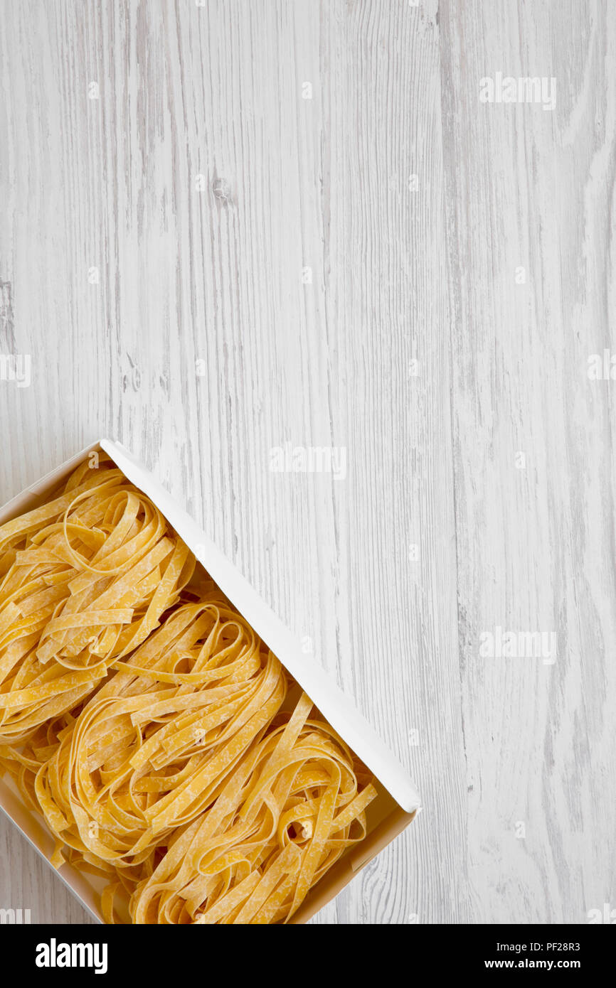 Uncooked pasta fettuccine in paper box on a white wooden background ...