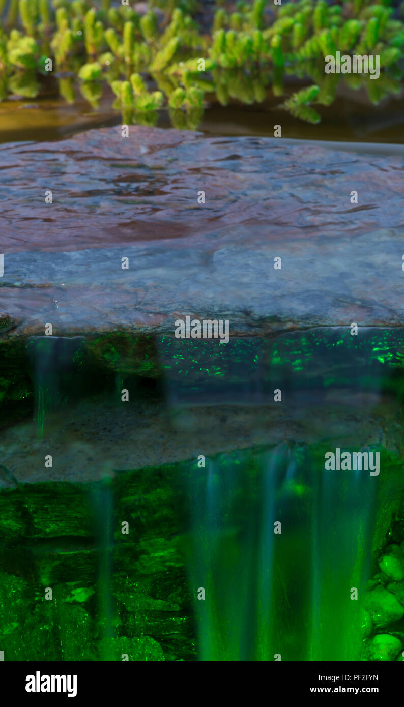 Green lights illuminate the flowing water on a small back yard ...