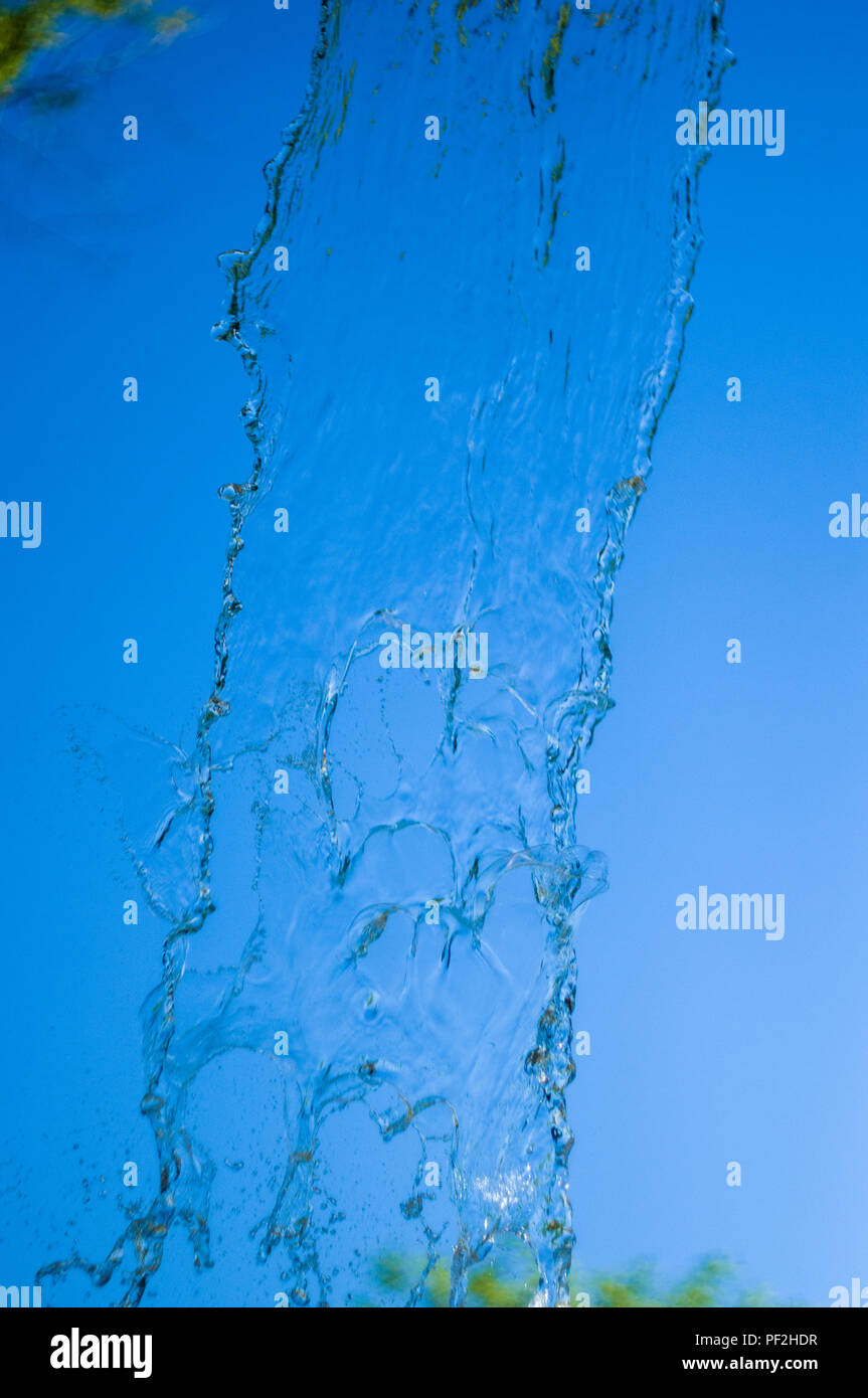 transparent falling water vertical flows against a blue sky and green ...