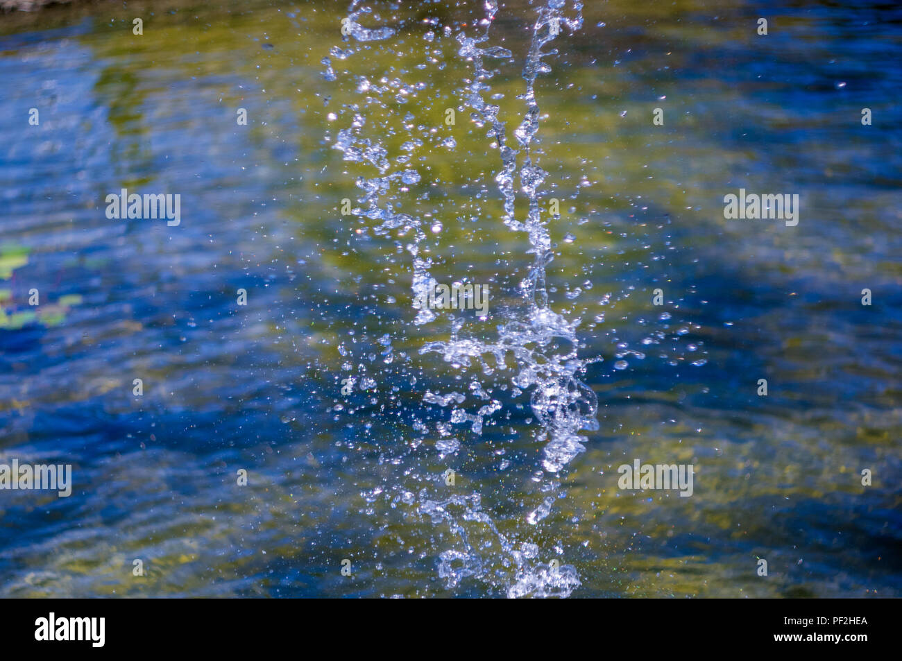 transparent falling water vertical flows against a blue sky and green ...