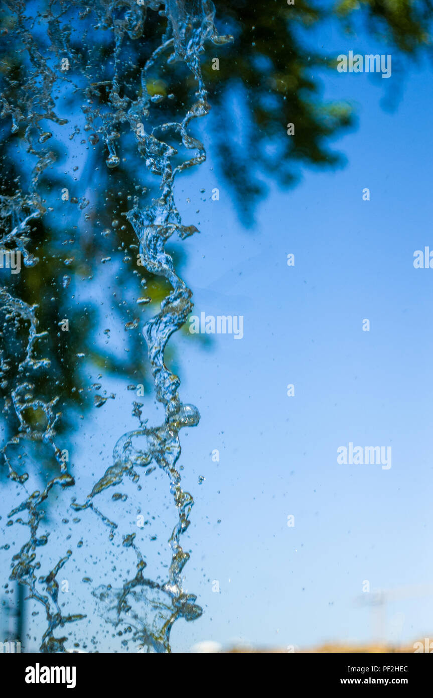 transparent falling water vertical flows against a blue sky and green ...