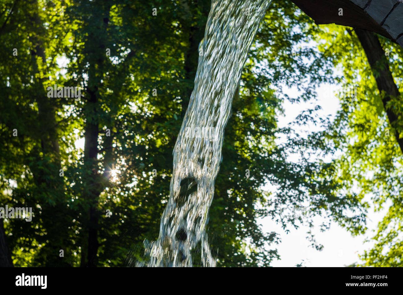 transparent falling water vertical flows against a blue sky and green ...