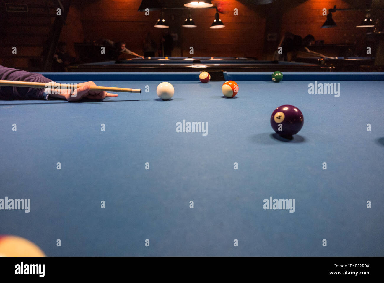 Men shoot pool in a dark pool hall with a blue felt table in the ...