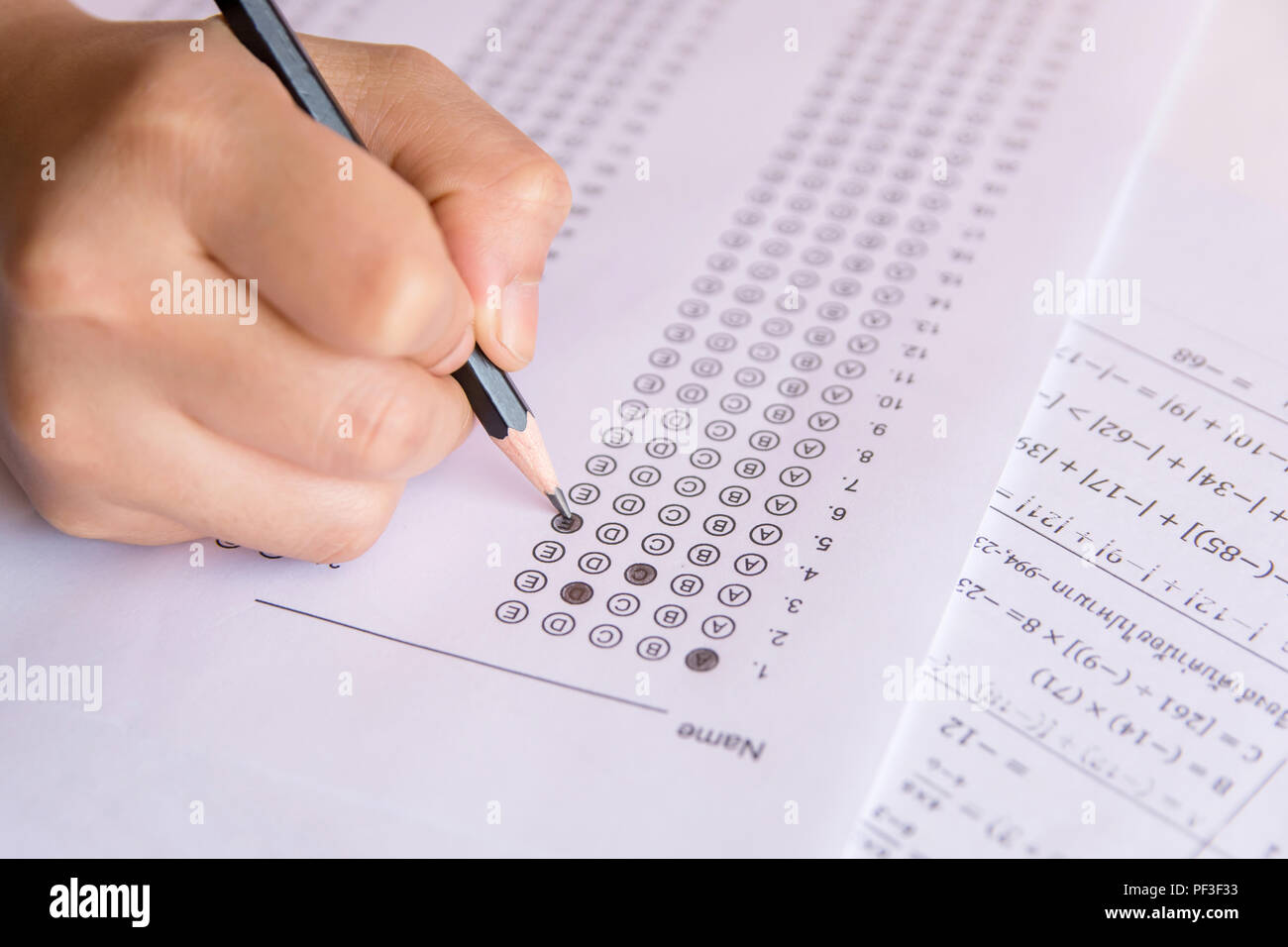 Students hand holding pencil writing selected choice on answer sheets ...