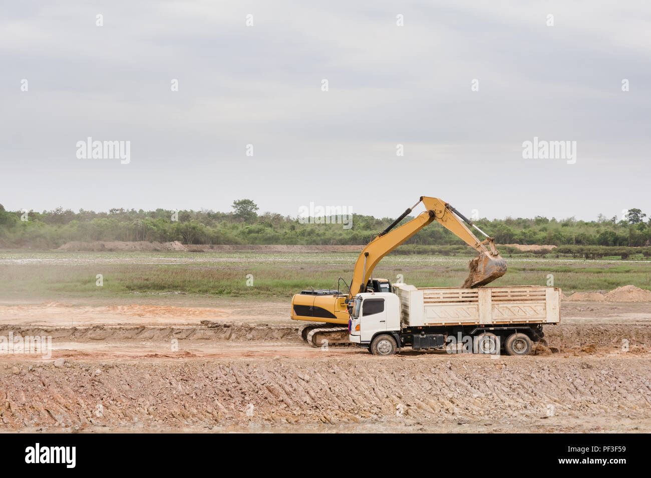 Yellow excavator machine loading soil into a dump truck at construction ...