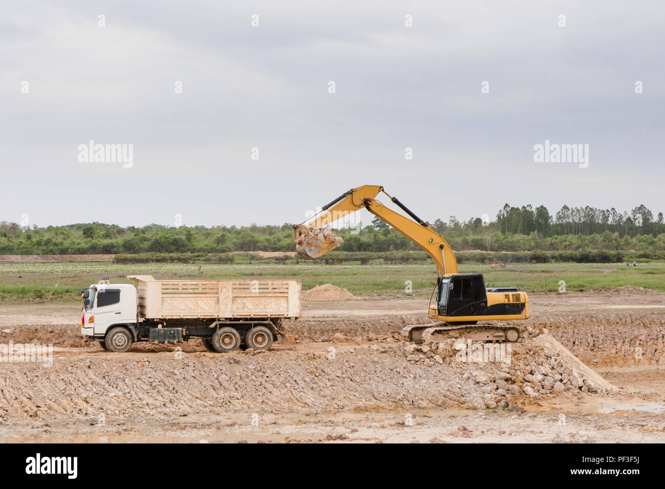 Yellow excavator machine loading soil into a dump truck at construction ...