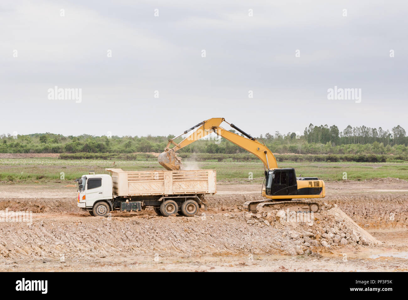 Yellow excavator machine loading soil into a dump truck at construction ...