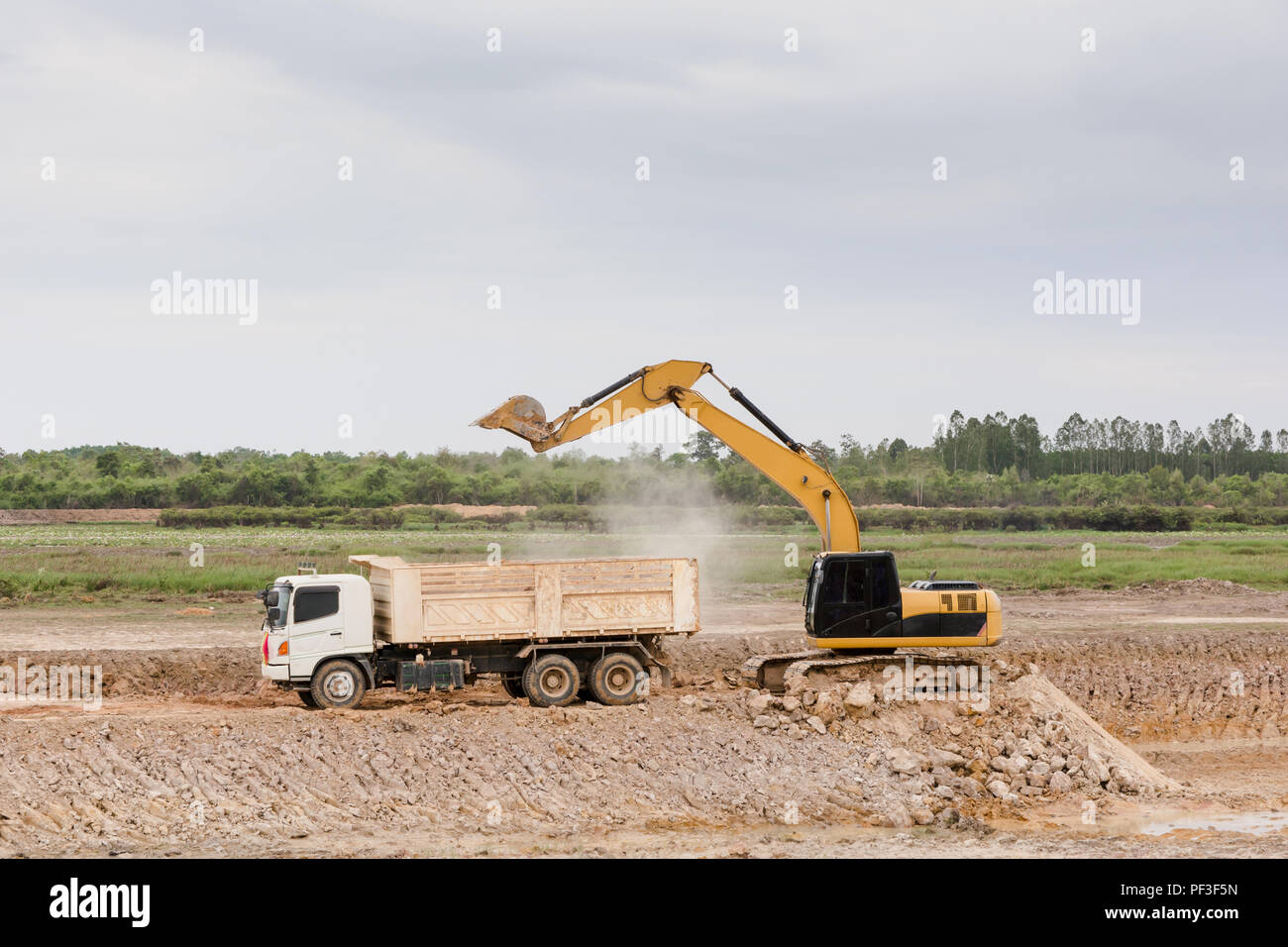 Yellow excavator machine loading soil into a dump truck at construction ...