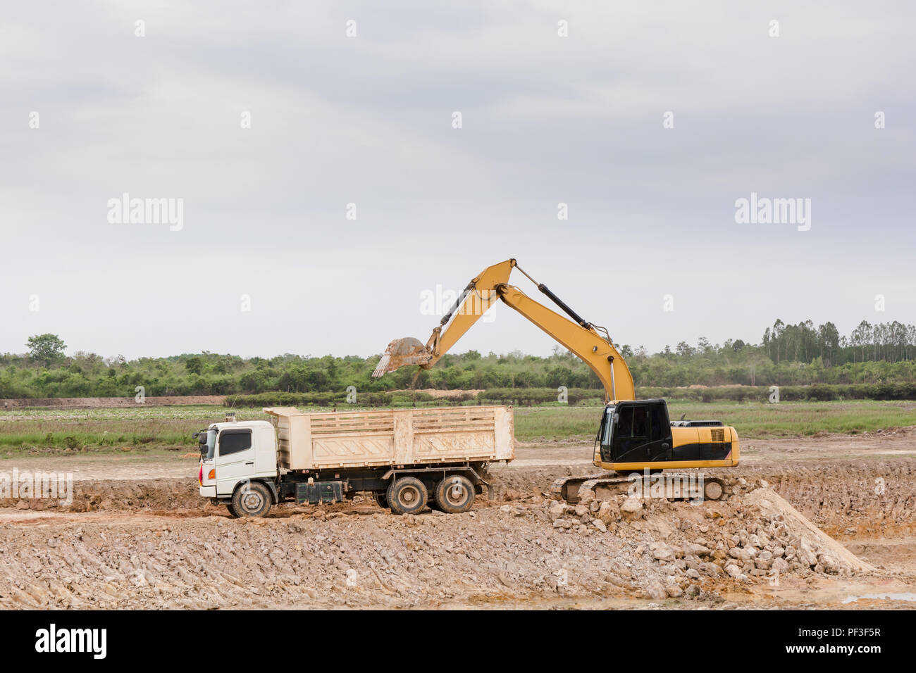 Yellow excavator machine loading soil into a dump truck at construction ...