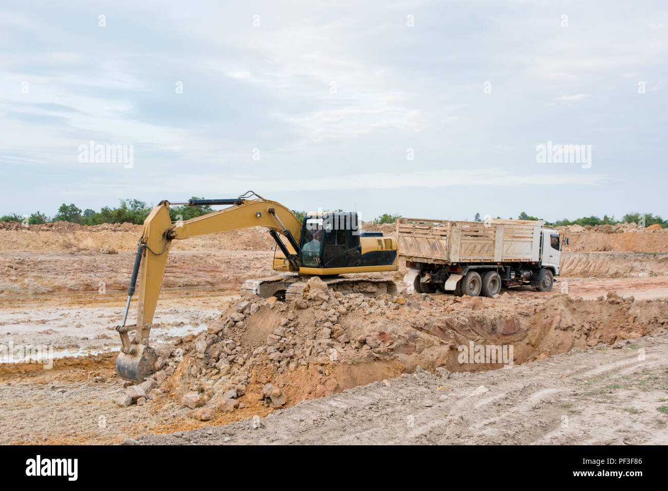 Yellow excavator machine loading soil into a dump truck at construction ...