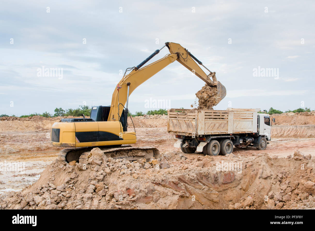 Yellow excavator machine loading soil into a dump truck at construction ...