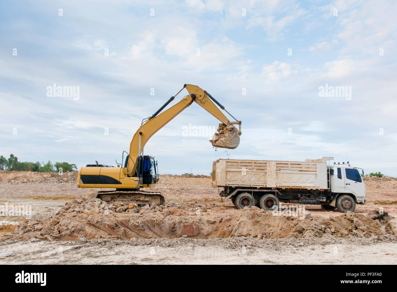 Yellow excavator machine loading soil into a dump truck at construction ...