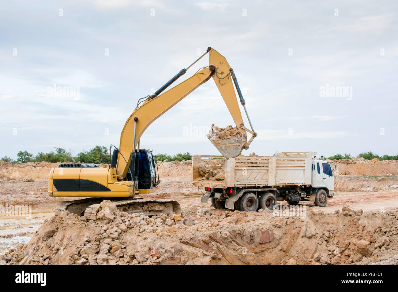 Yellow excavator machine loading soil into a dump truck at construction ...