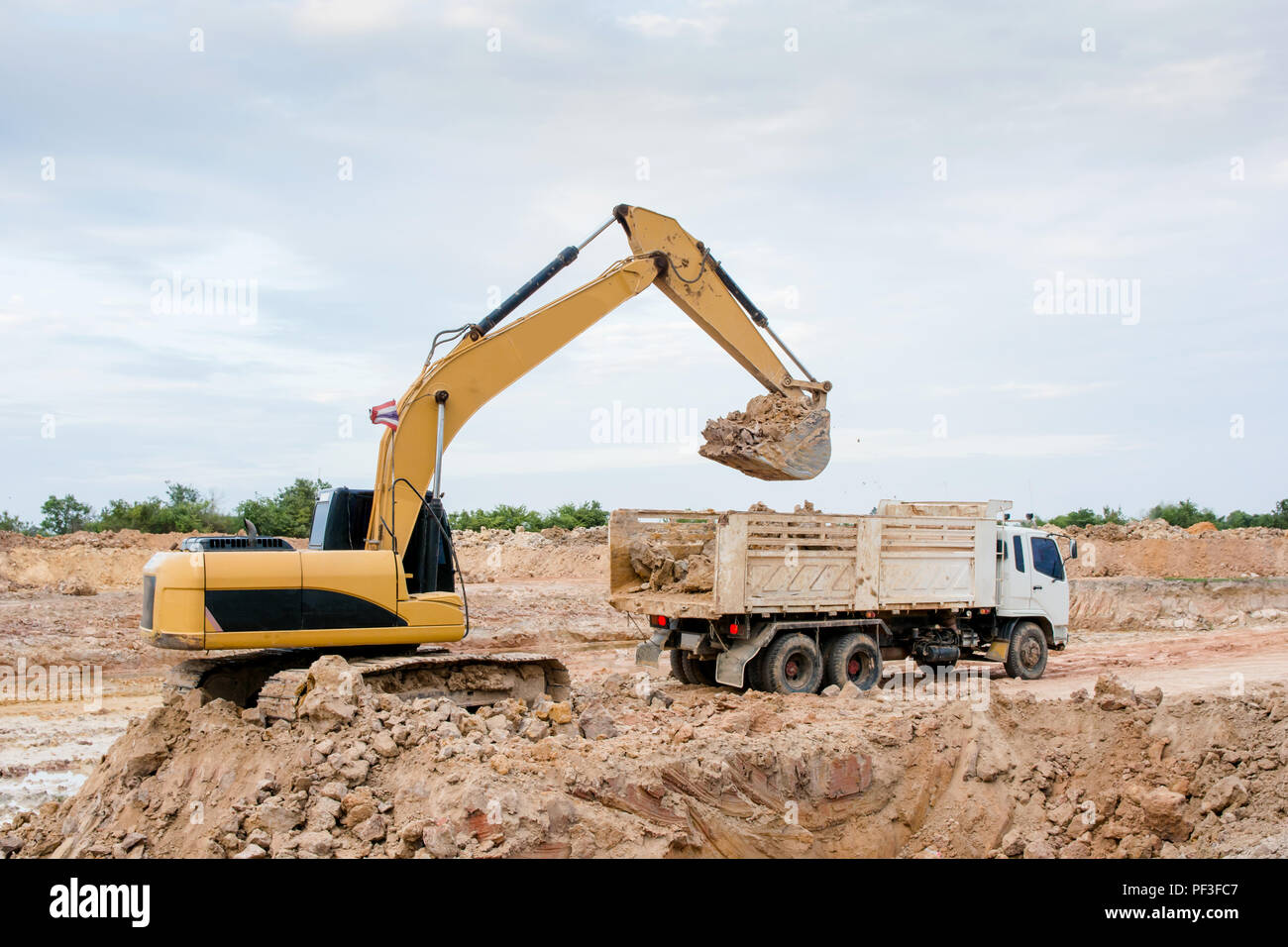 Yellow excavator machine loading soil into a dump truck at construction ...