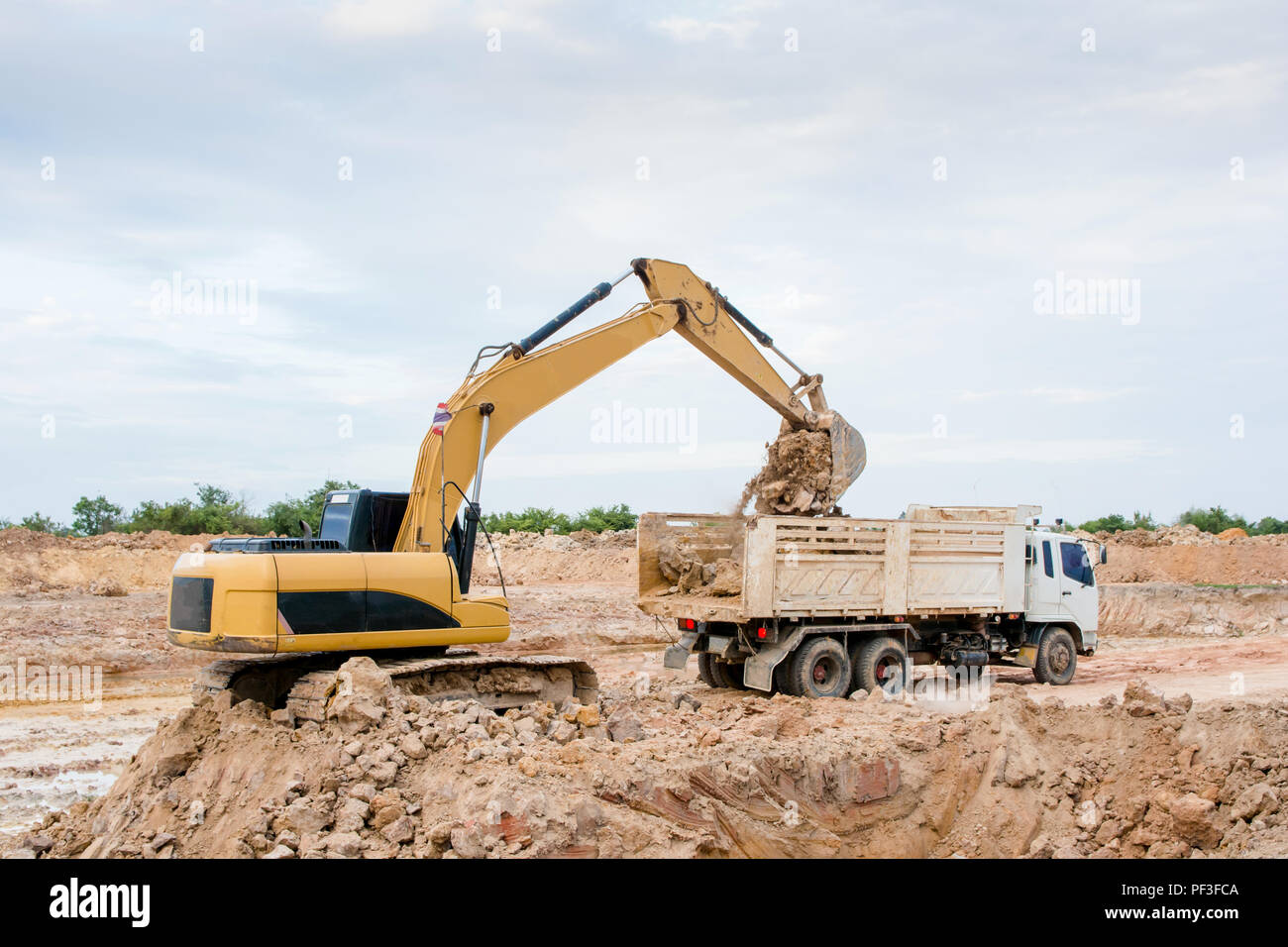 Yellow excavator machine loading soil into a dump truck at construction ...