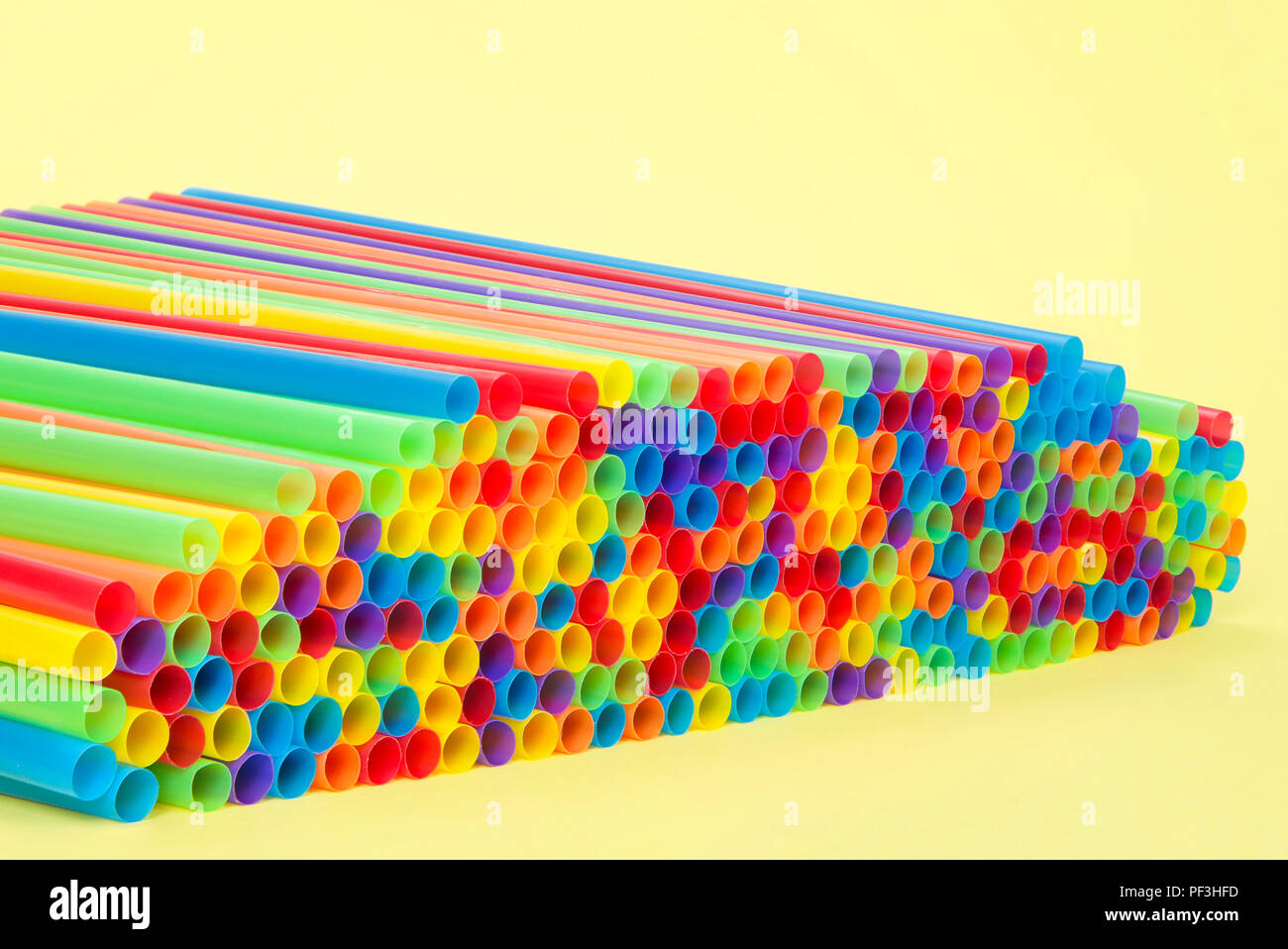 Hundreds of colorful plastic straws laying on yellow surface with ...