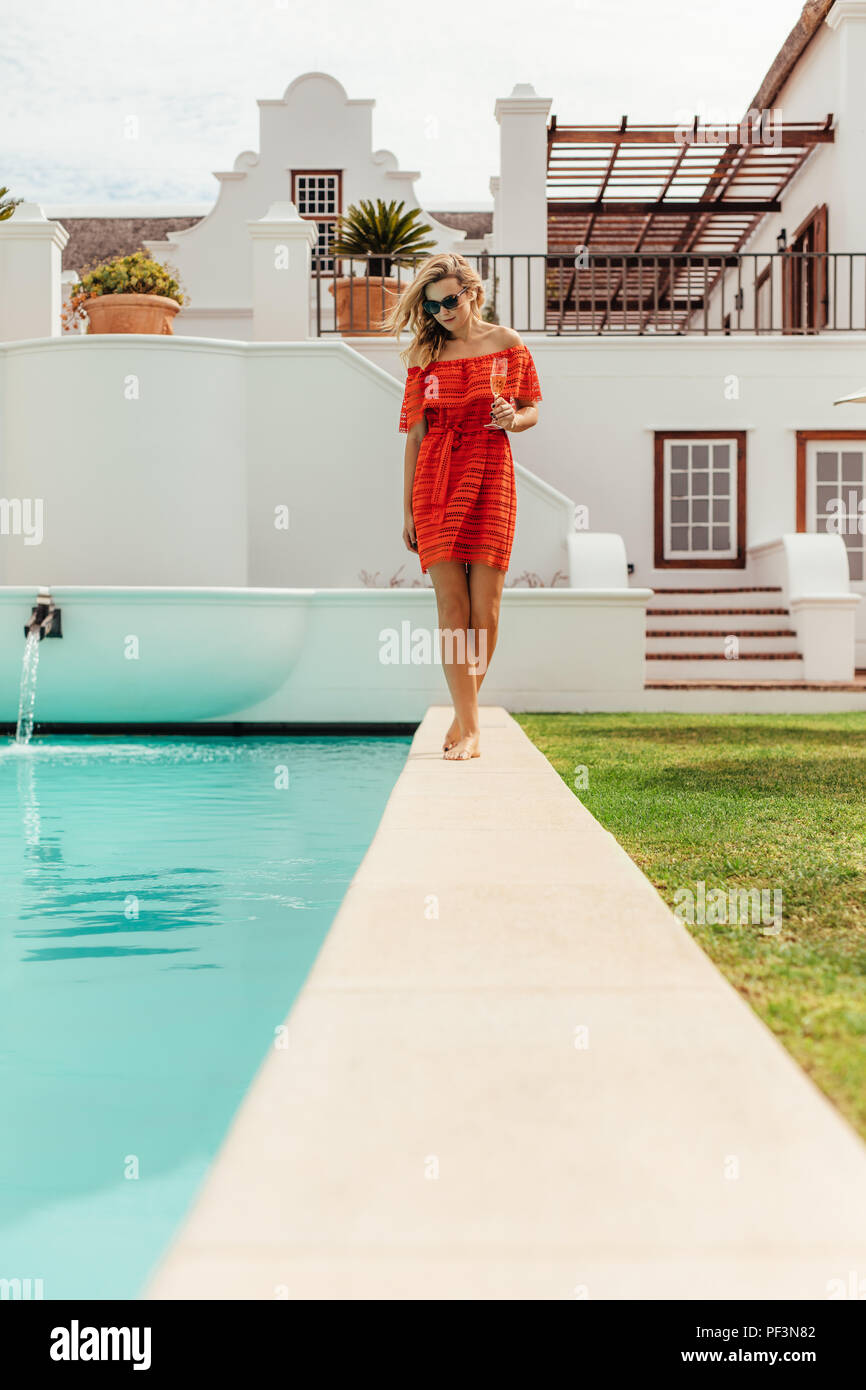 Beautiful woman walking on the edge of the swimming pool with glass of ...