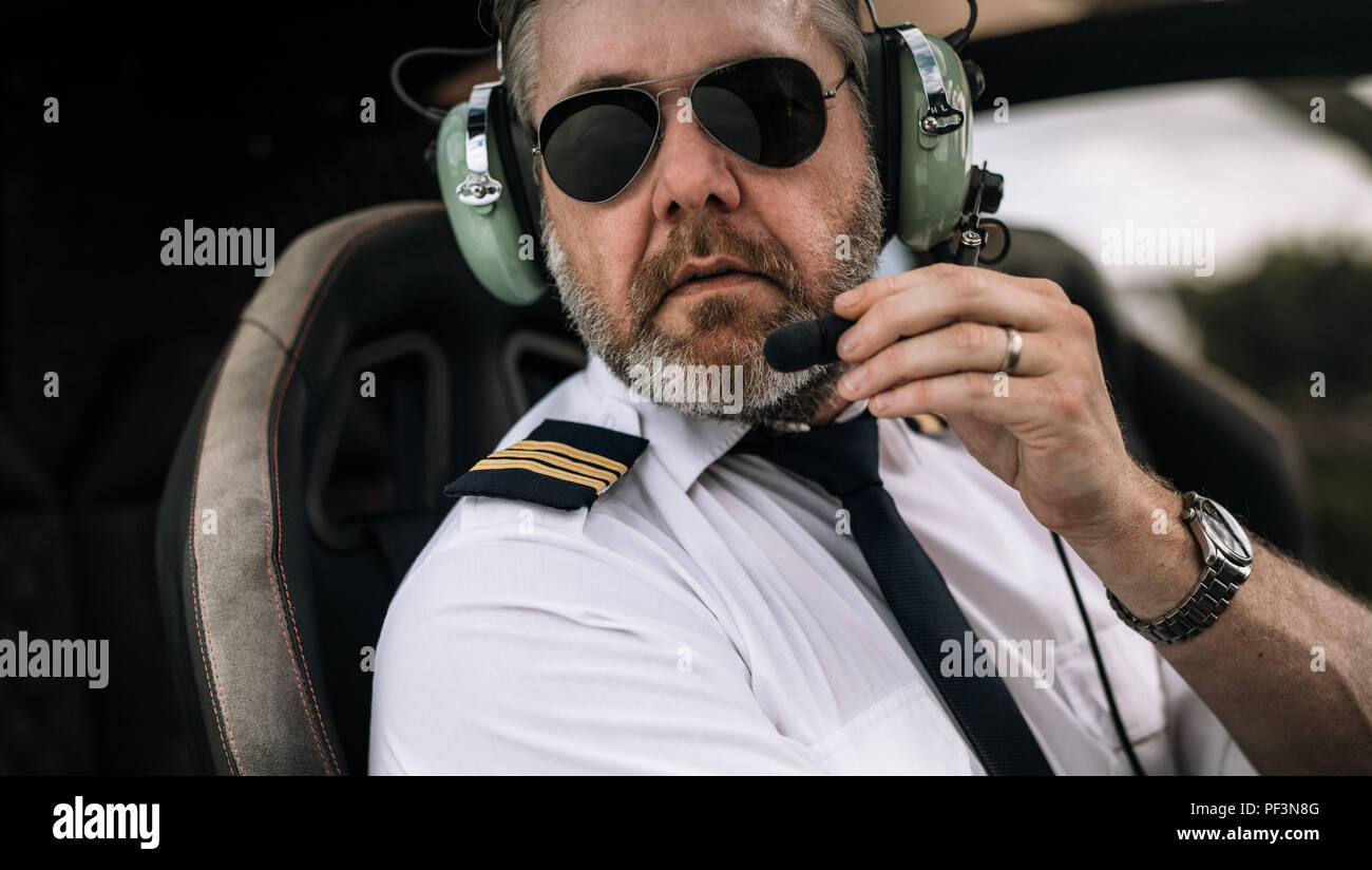 Mature male helicopter pilot with headset in the private helicopter ...
