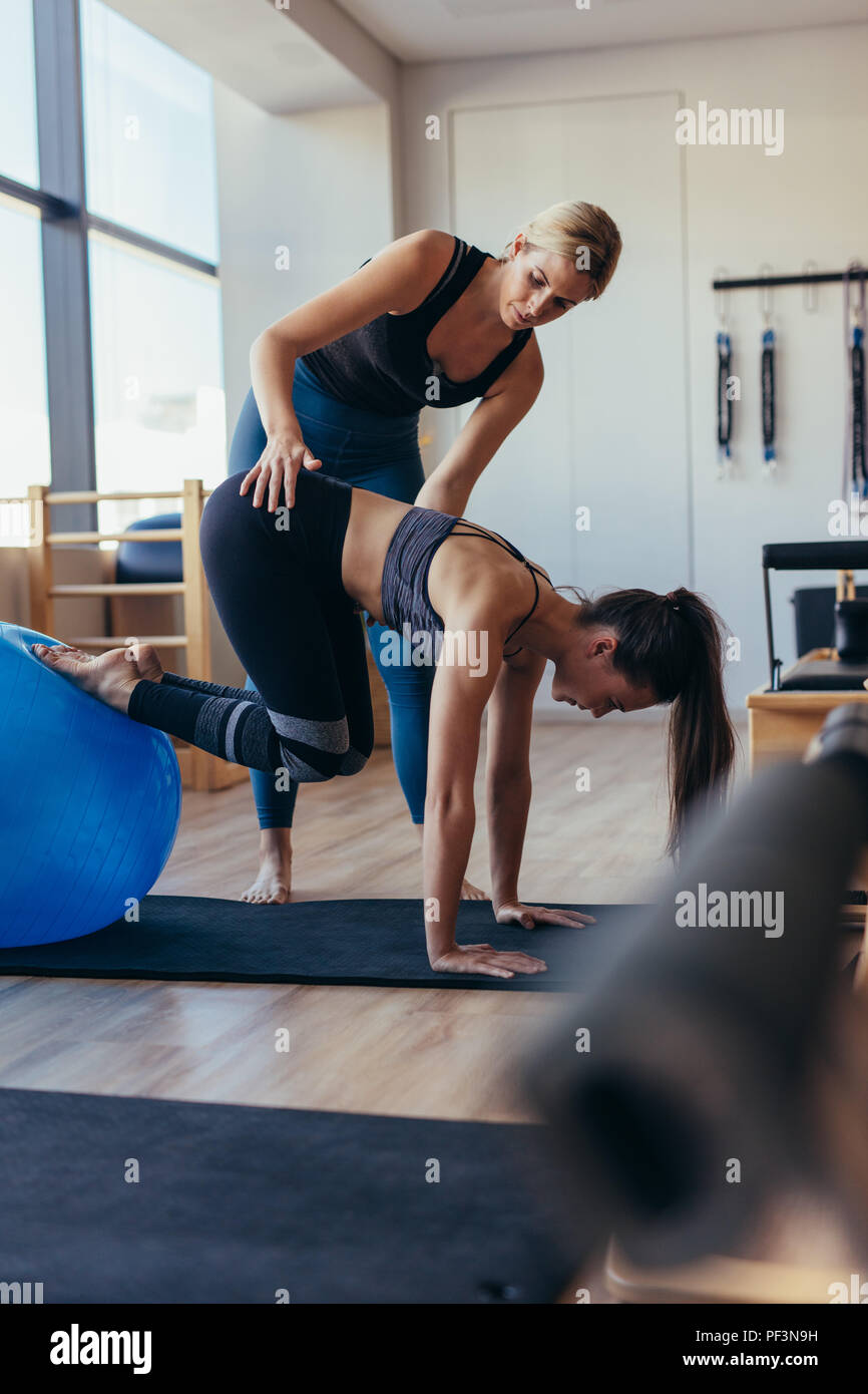 Pilates instructor helping a woman balance her feet on a fitness ball ...