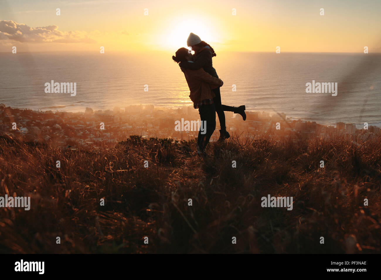 Silhouette of young man carrying his girlfriend on the mountain peak ...