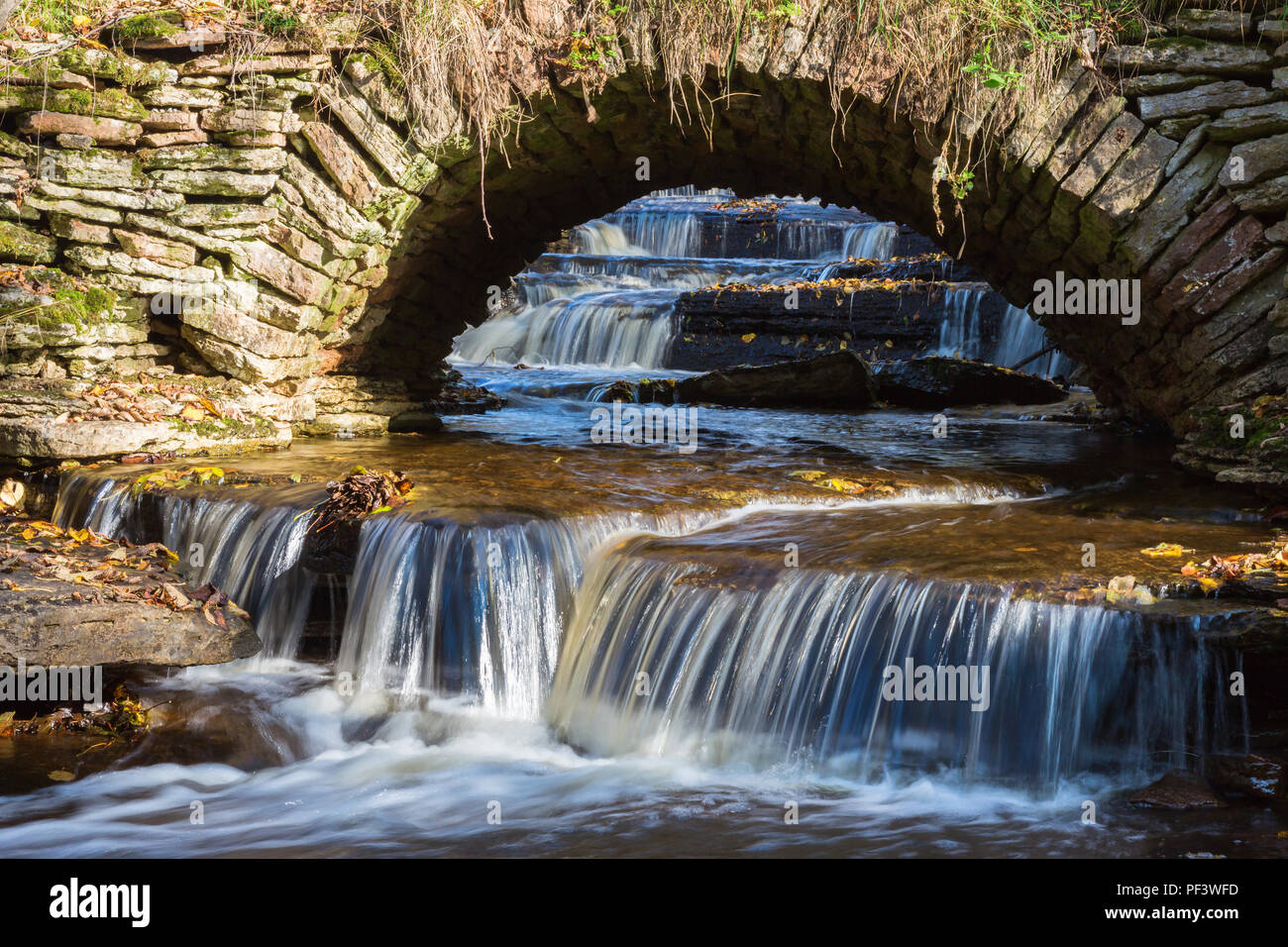 Waterfall flowing under an old arch bridge Stock Photo - Alamy