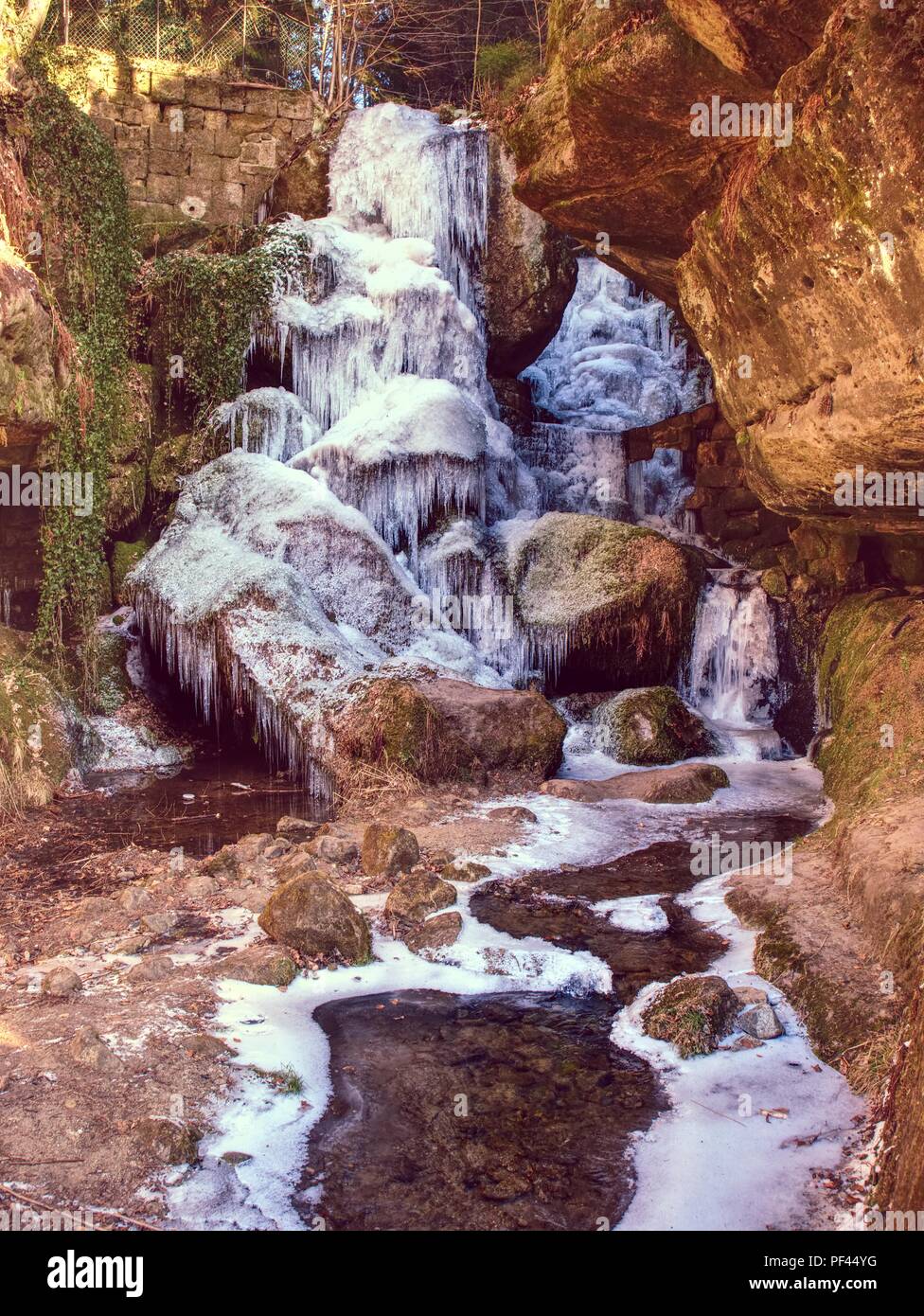 Winter frozen waterfall. Small pond and snowy boulders bellow cascade ...
