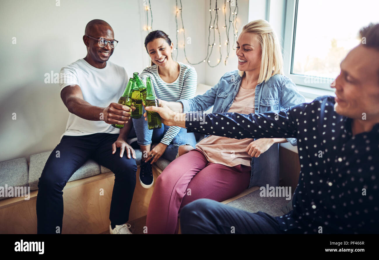 Diverse group of young work colleagues laughing and cheering with beers ...